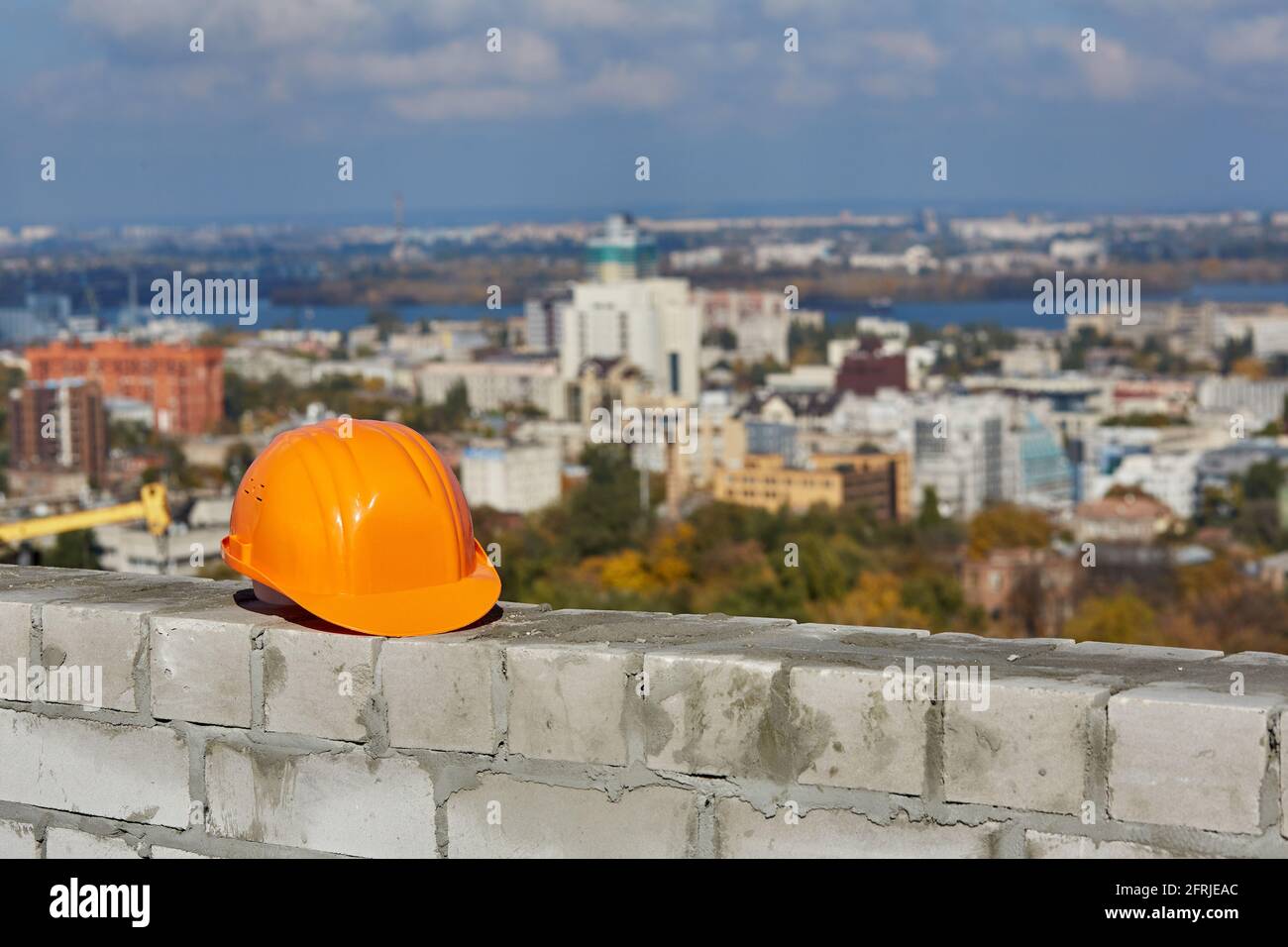 Orange plastic safety helmet is on a brick wall. Roof of modern ...