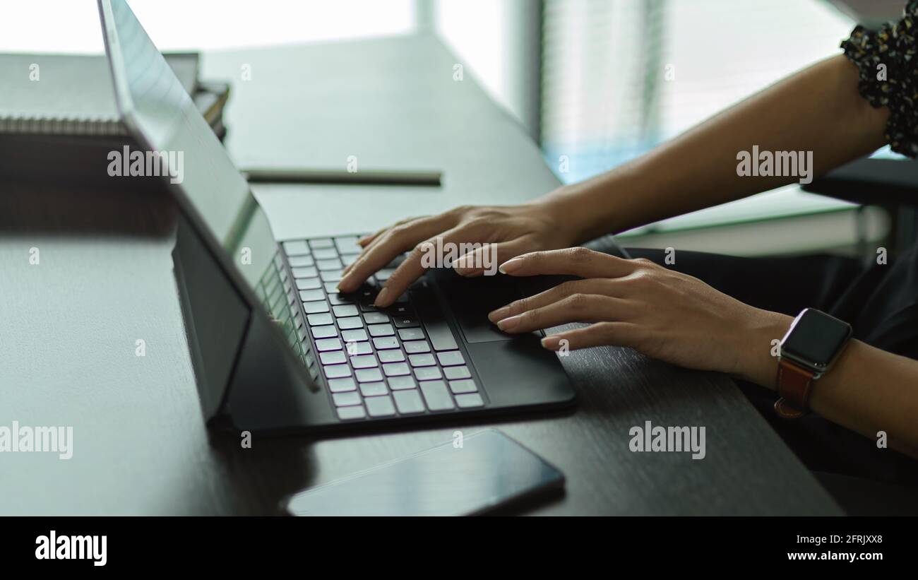 Side view of female hands typing on tablet keyboard on worktable in ...