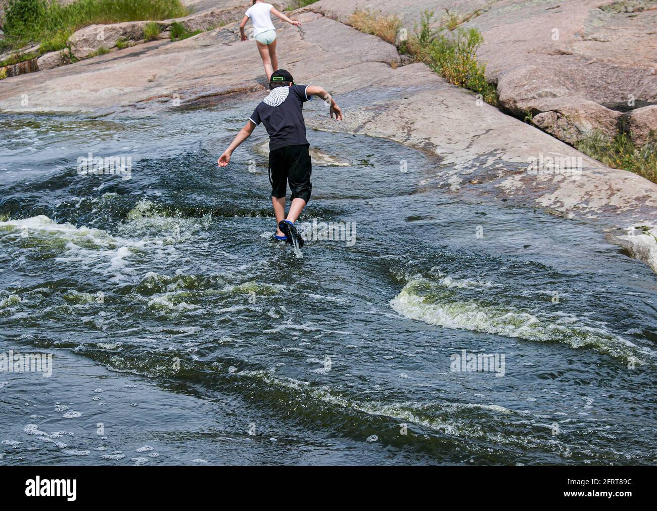 People are crossing the fast flowing river. Tourists walk over rocks in ...