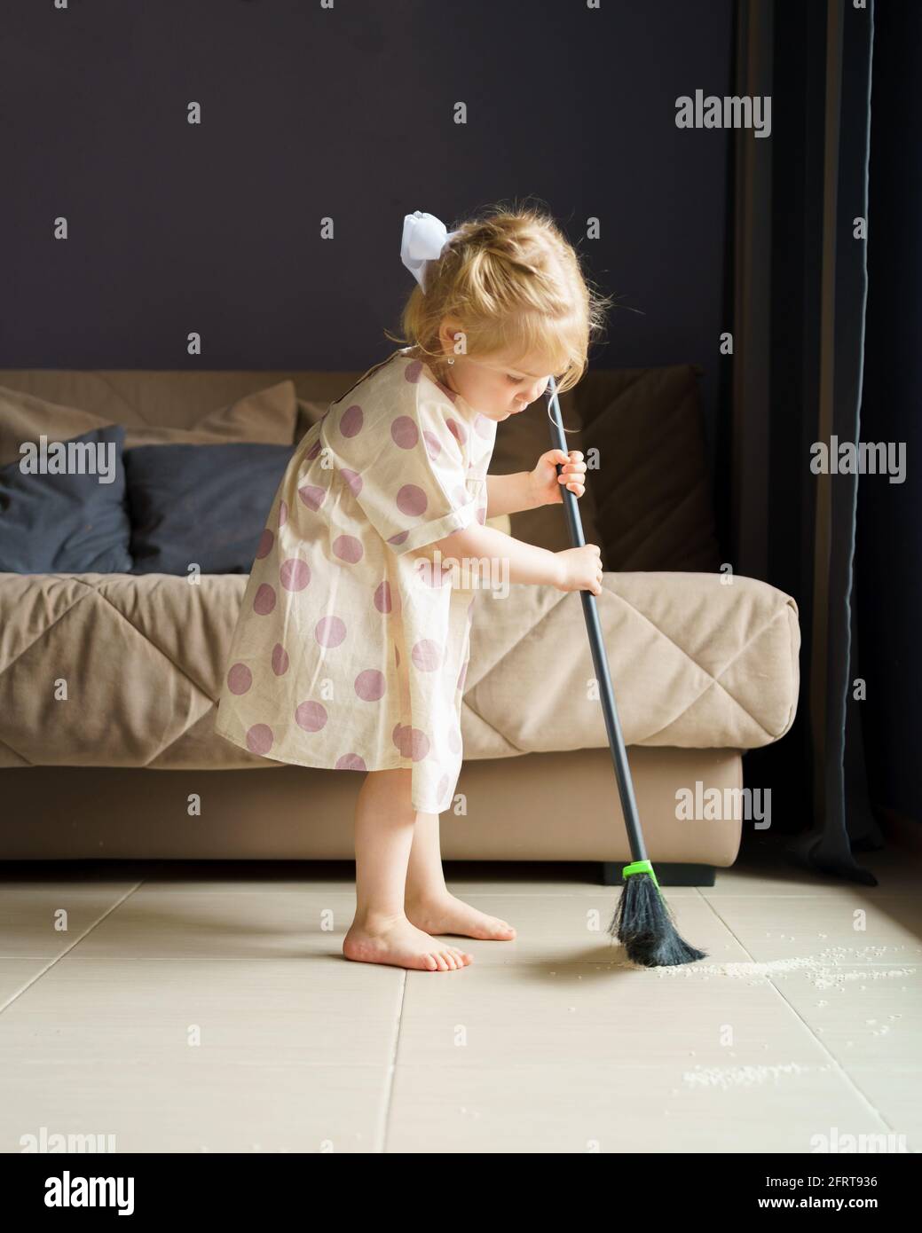 Adorable little girl with golden hair in polka dot linen dress sweeping ...