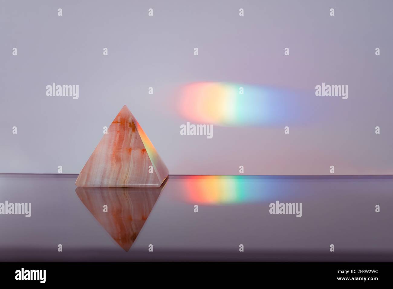 Agate pyramid with a rainbow streak background on a reflective surface ...