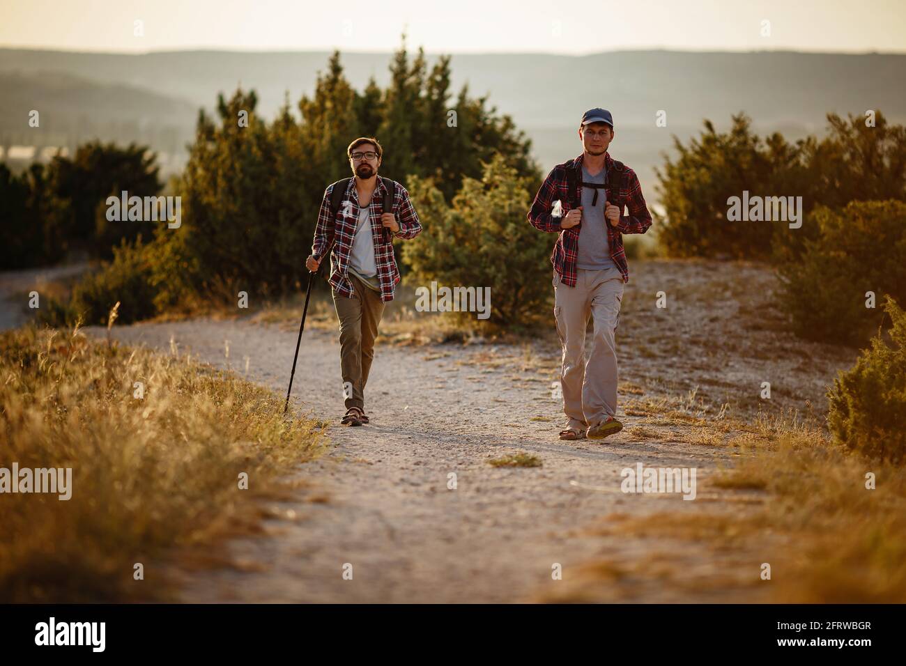two men hikers enjoy a walk in nature, sunset time in summer. enjoying ...