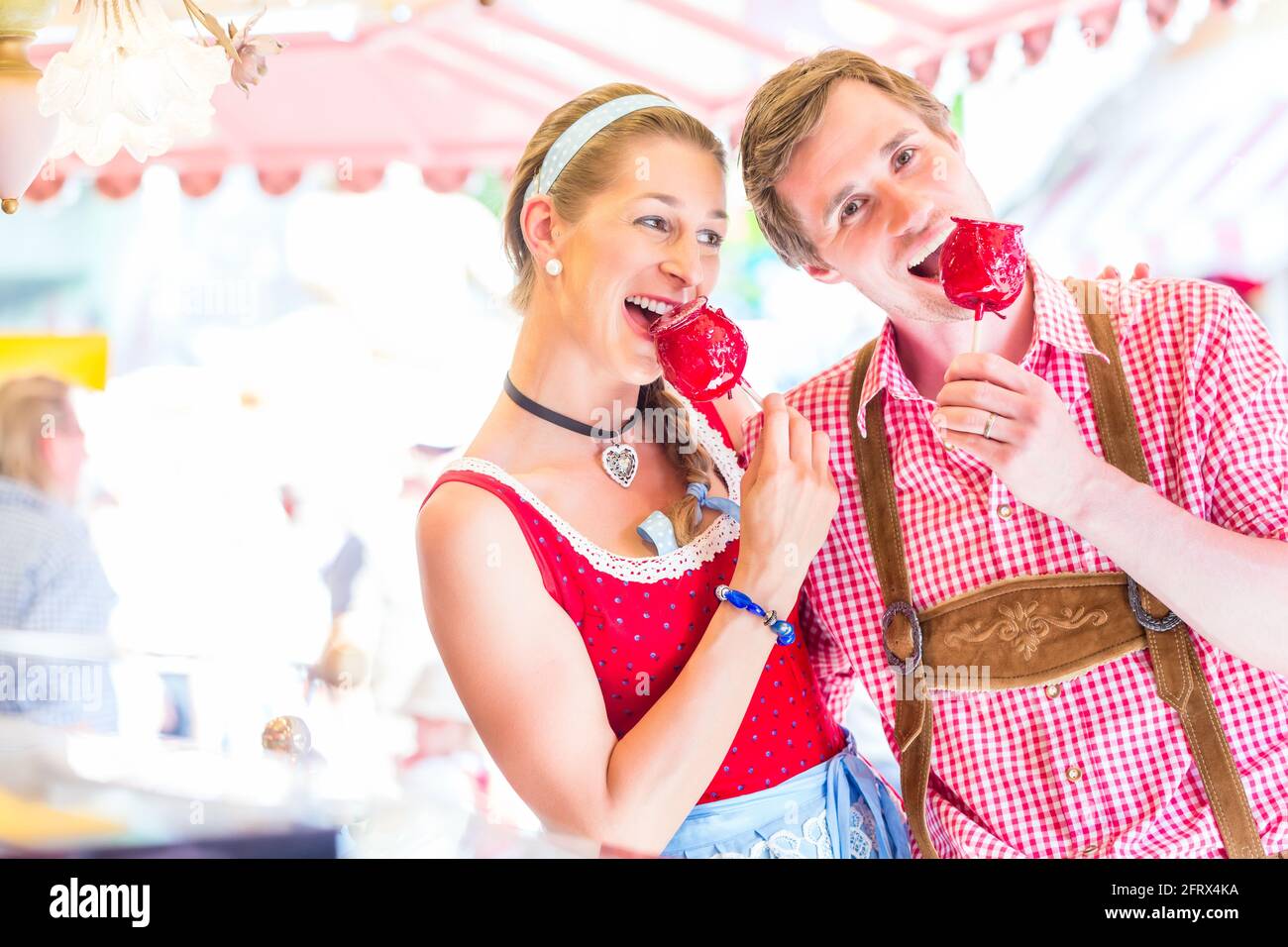 Couple visiting together Bavarian fair in national costume eating candy ...