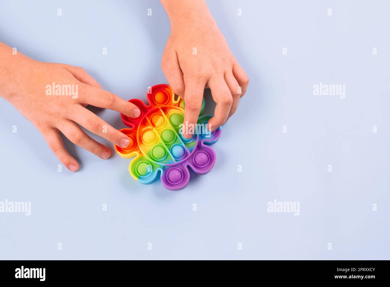 Close up of boy's hands using rainbow pop it fidget toy on blue ...
