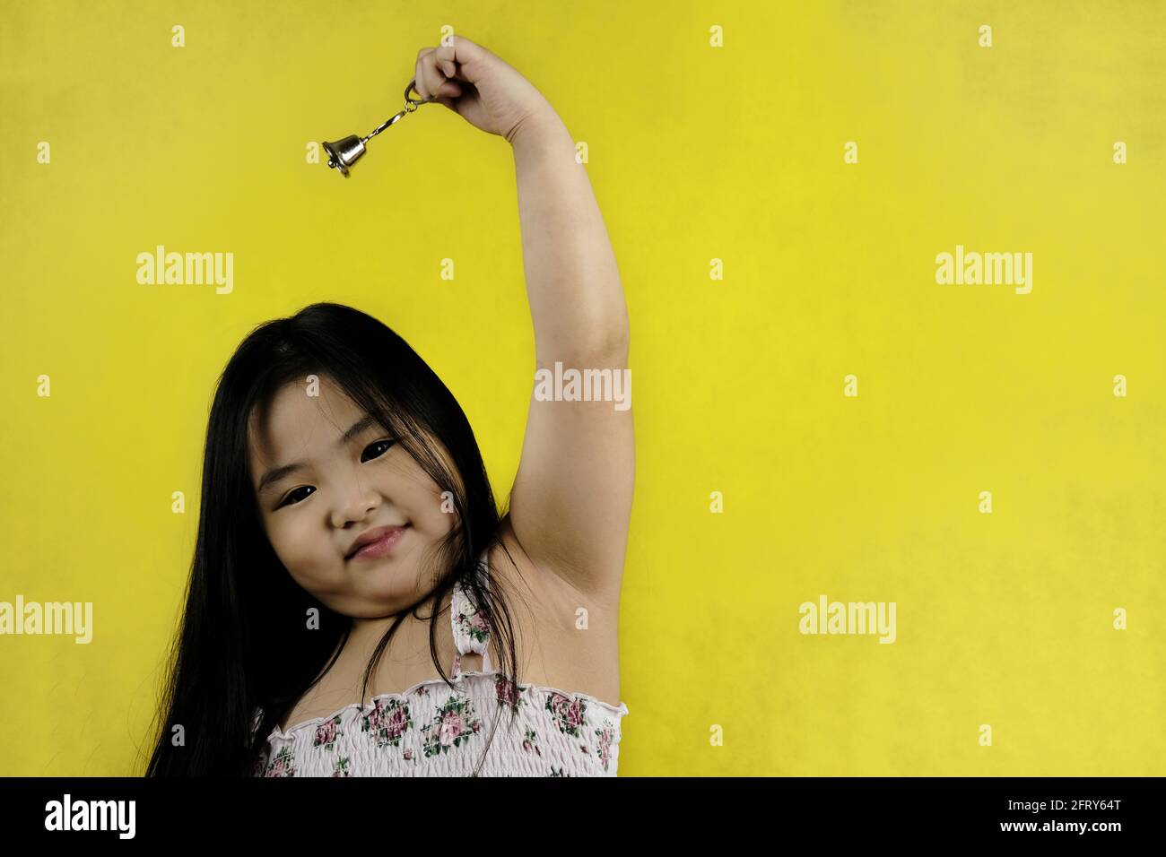 Ring a bell. A cute young Asian girl holding a tiny metal bell, ringing ...