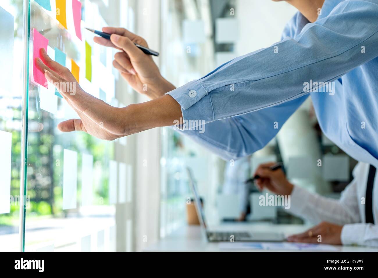 Young businesspeople use their hand point to color sticky note on glass ...