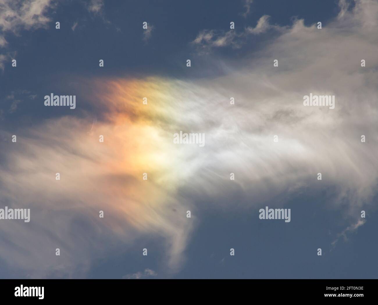 Small white cloud with colours of a rainbow of refracted light at one ...