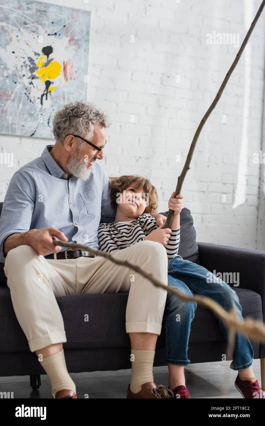 Smiling grandfather and boy holding wooden twigs at home Stock Photo ...