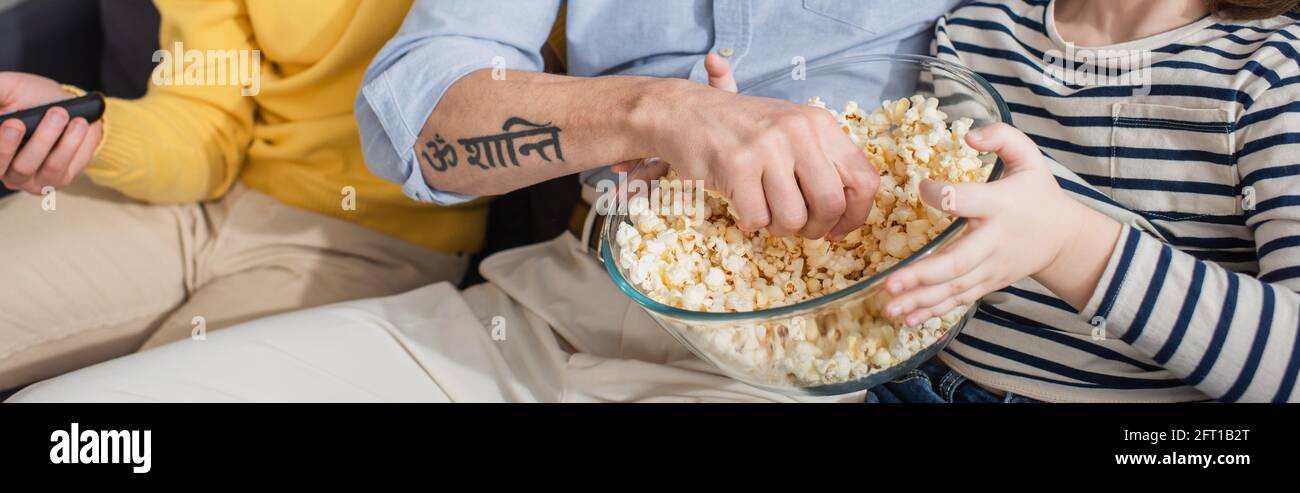 Cropped view of boy holding popcorn near parents with remote controller ...