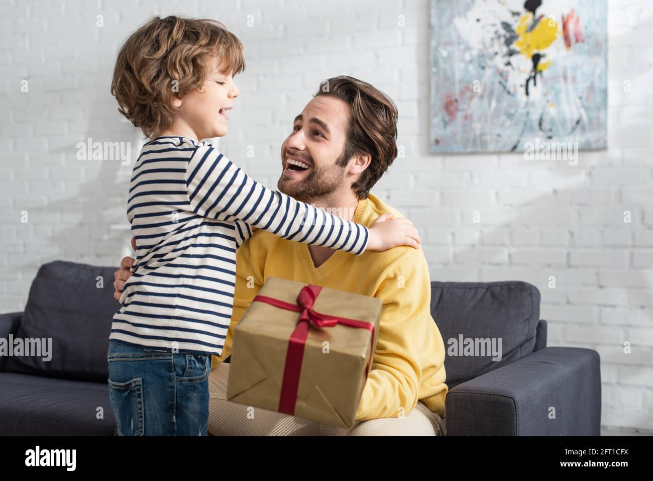 Cheerful kid hugging father with present on blurred foreground Stock ...
