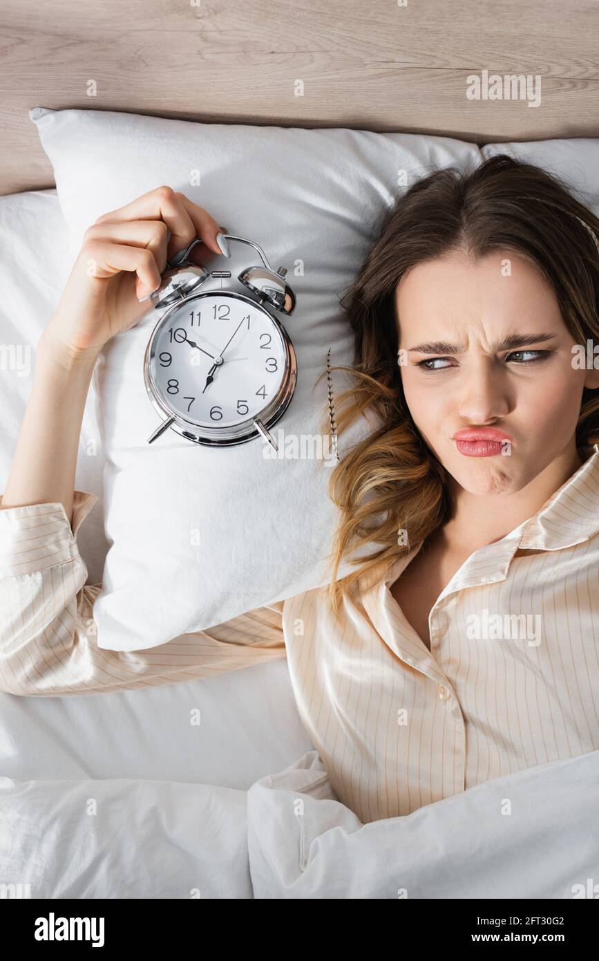 Top view of sad woman holding alarm clock on bed Stock Photo - Alamy