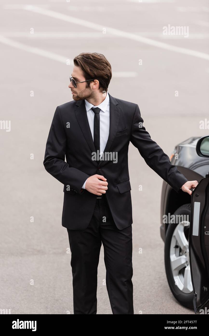 bearded bodyguard in suit and sunglasses with security earpiece opening ...