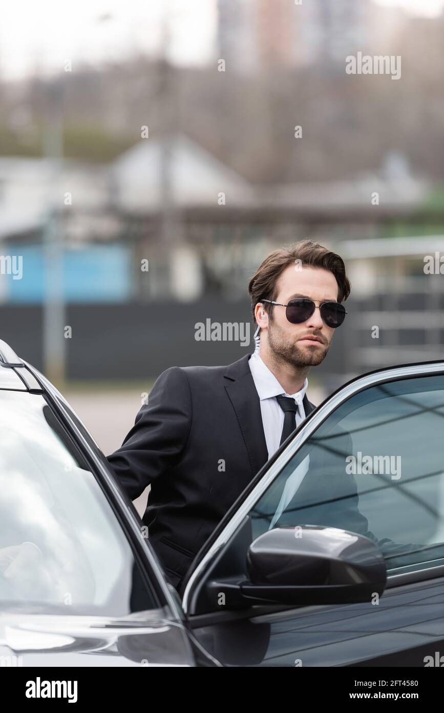 bearded bodyguard in suit and sunglasses with security earpiece sitting ...