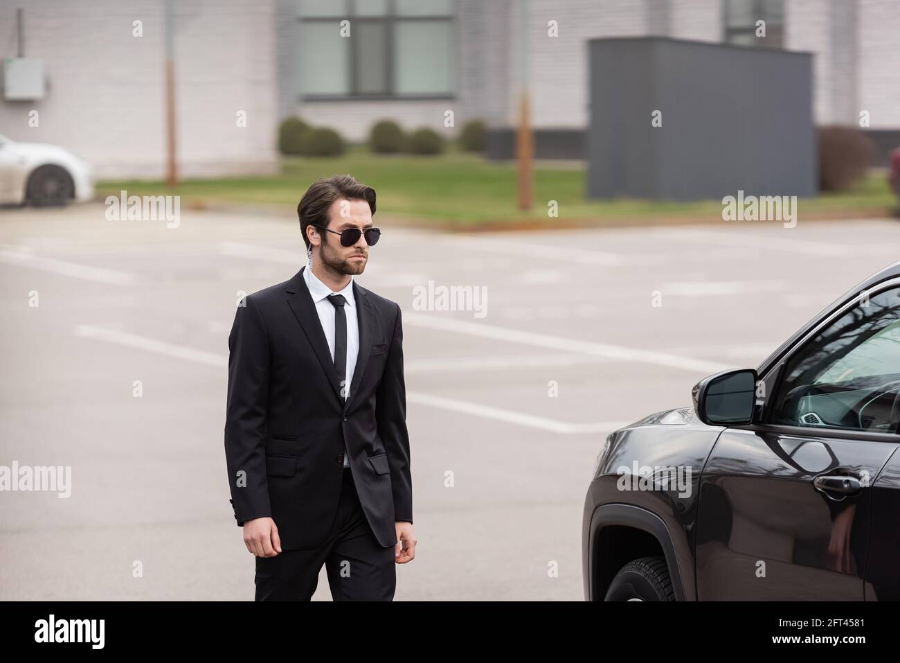 bearded bodyguard in suit and sunglasses with security earpiece walking ...