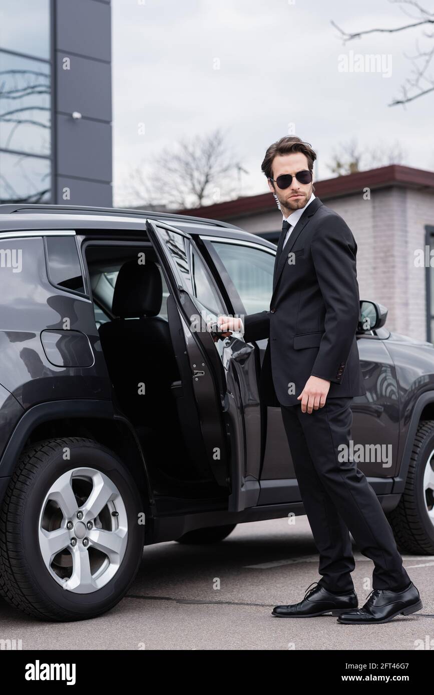 bearded bodyguard in suit and sunglasses with security earpiece opening ...