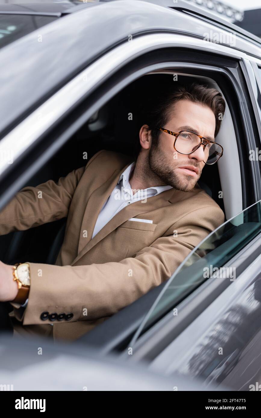 bearded man in glasses looking through car window while driving auto ...