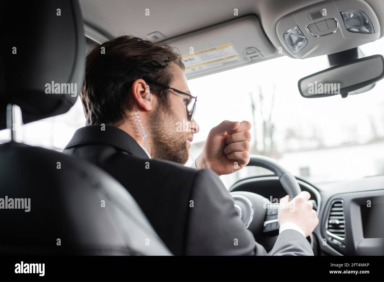 bearded bodyguard in sunglasses and security earpiece talking while ...