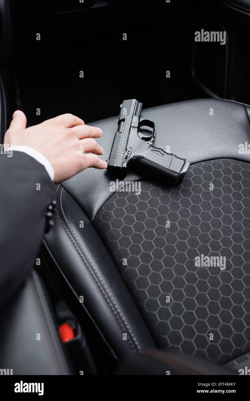cropped view of bodyguard reaching gun on seat of modern automobile ...