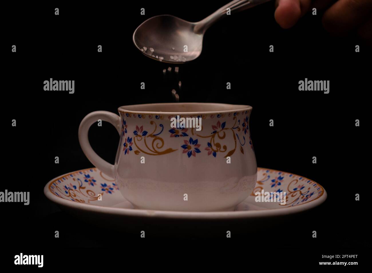 Hand adding a spoonful of sugar to a cup of Indian masala tea against a ...