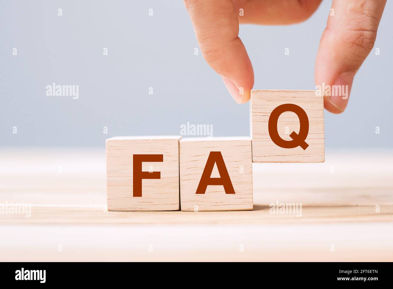 Hand holding wooden cube blocks with FAQ text (frequently asked ...