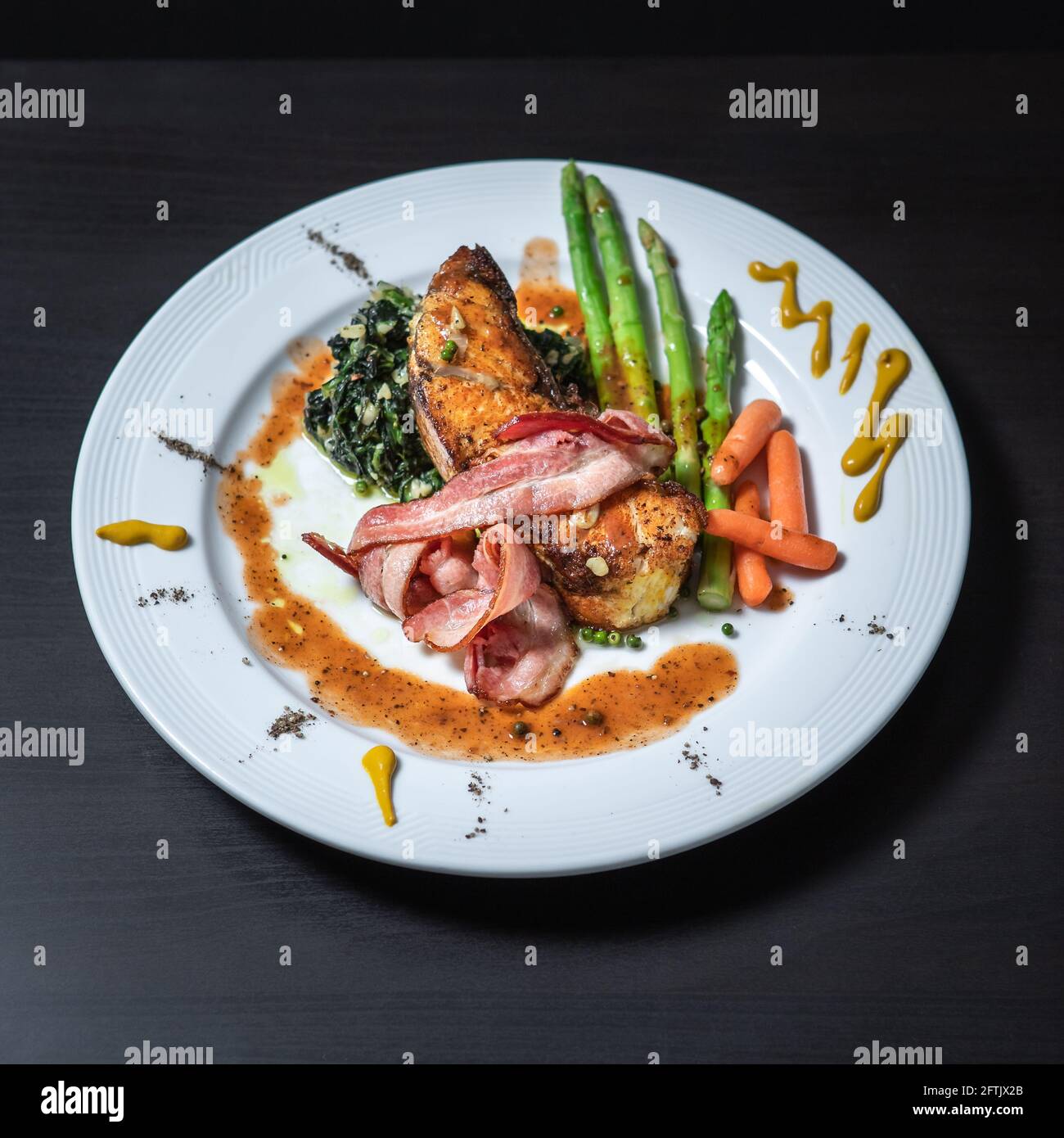 A Dish of Sea Bass Filet Steak with Bacon, Spinach, Asparagus, and Baby ...
