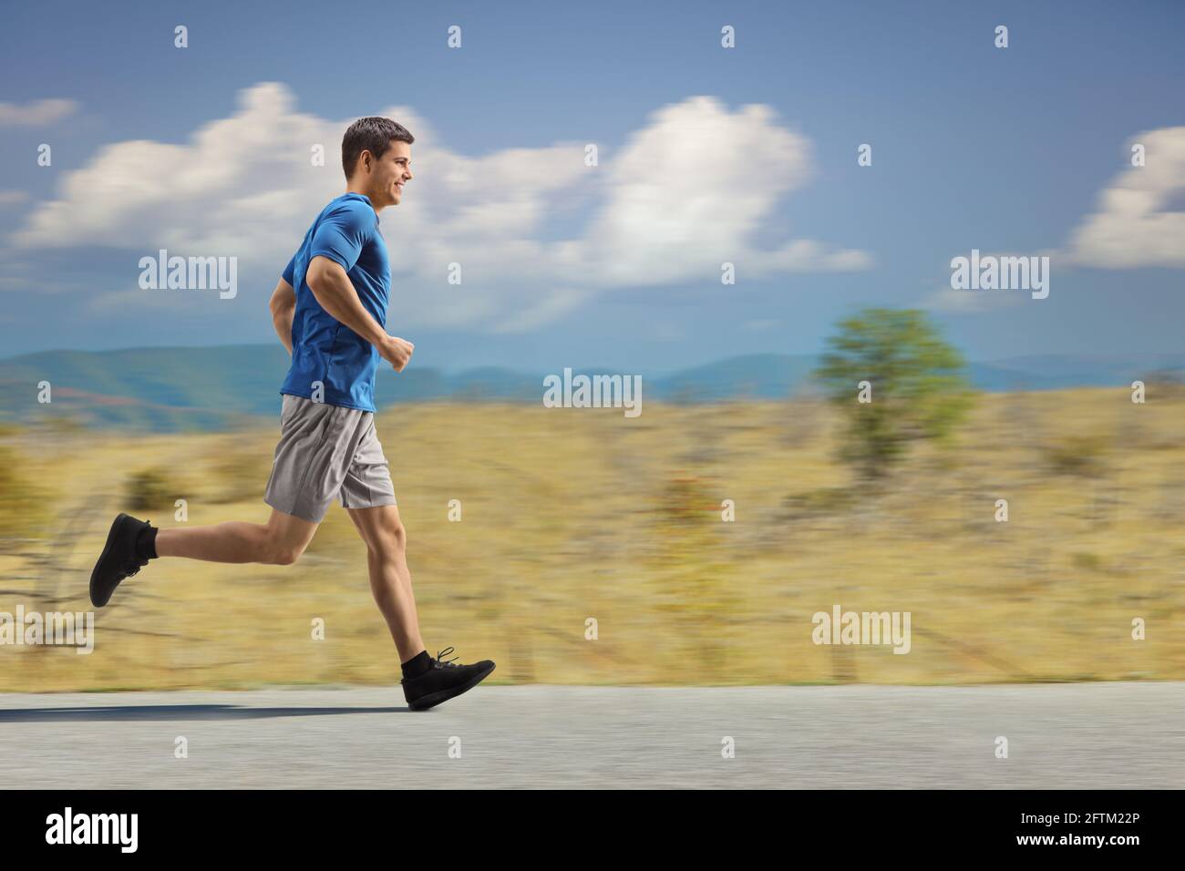 Full length profile shot of a guy in sports clothes running in a rural ...