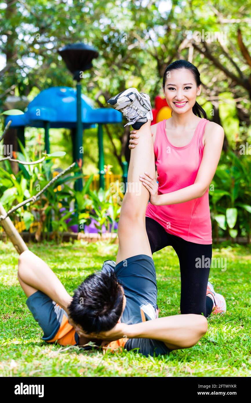 Asian Chinese woman helping man with stretching exercises in park for ...