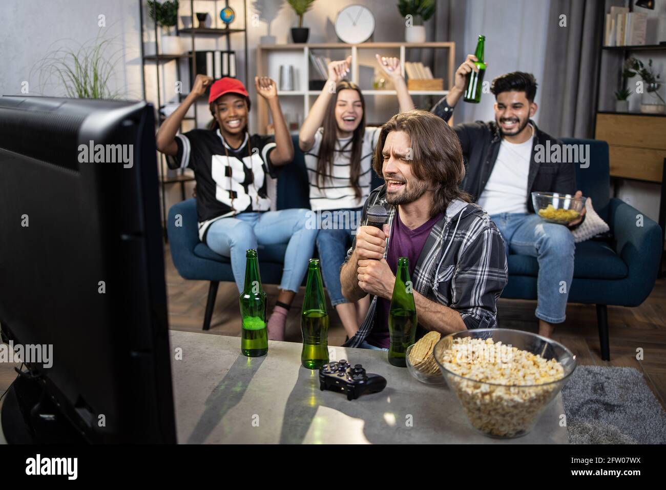 Group of four multicultural people singing karaoke, drinking beer and ...