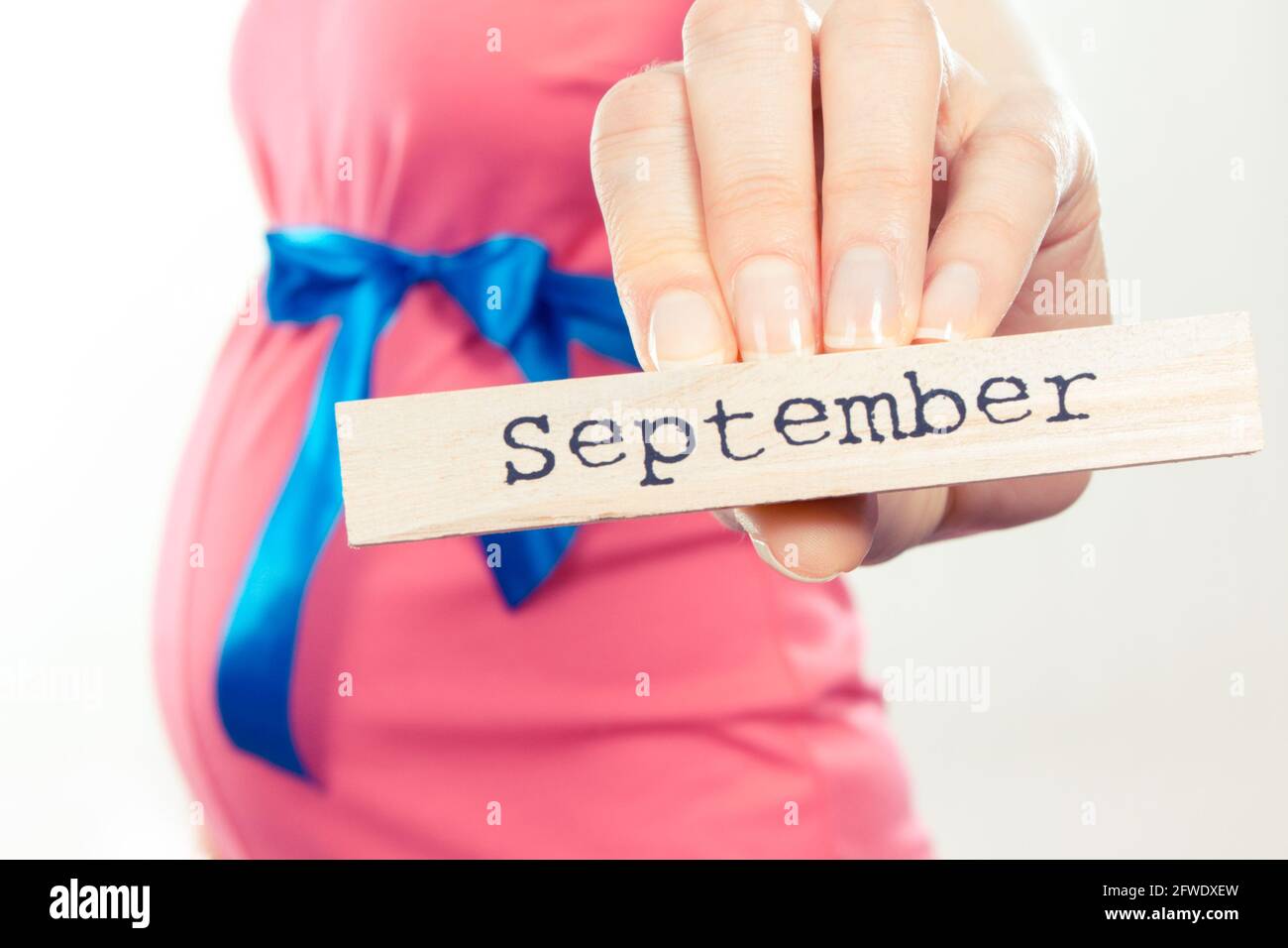 Woman in pregnant wearing pink dress with blue ribbon and showing word ...