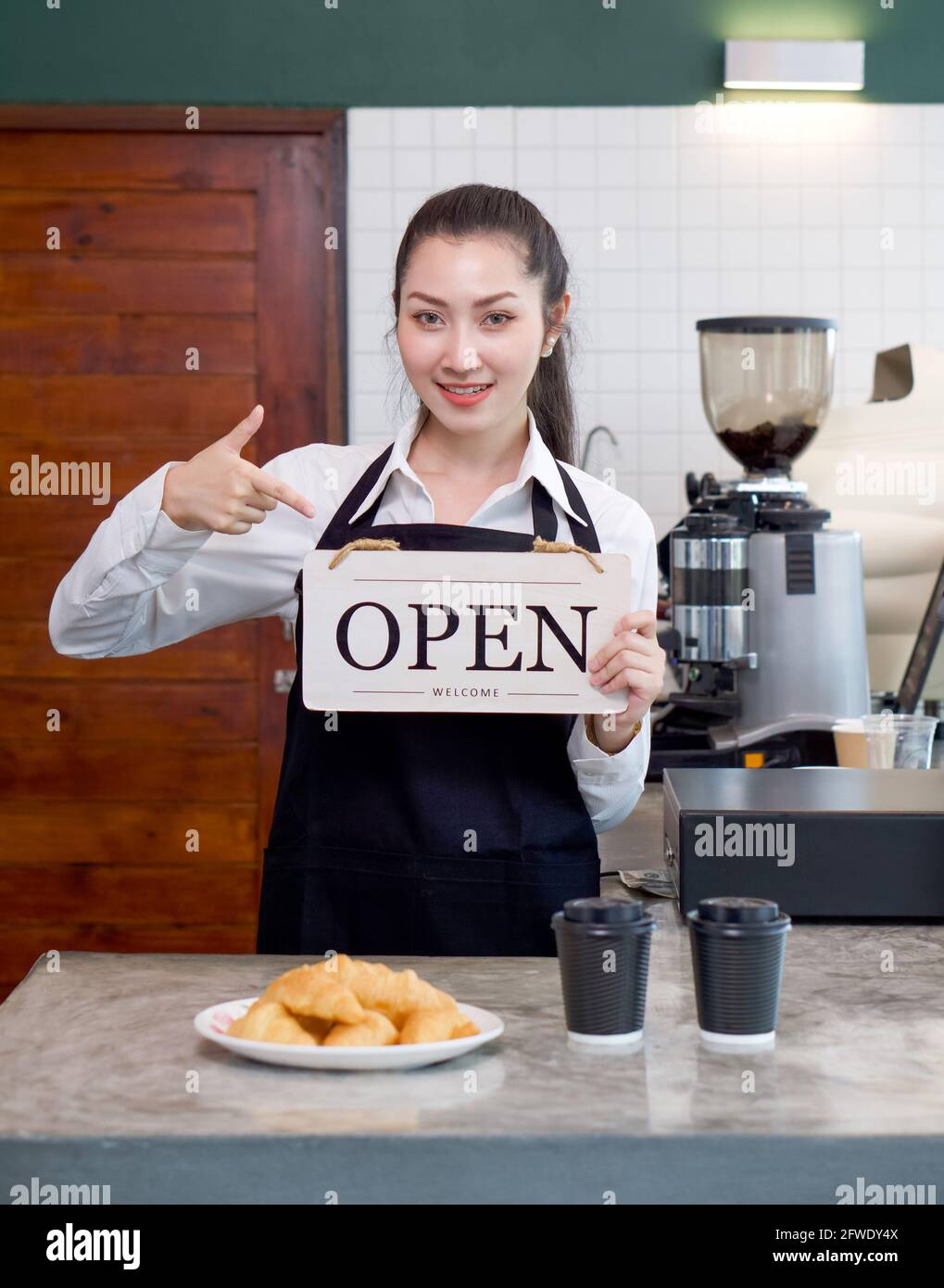 Young asian shopkeeper with a smile holds an OPEN sign in front of a ...