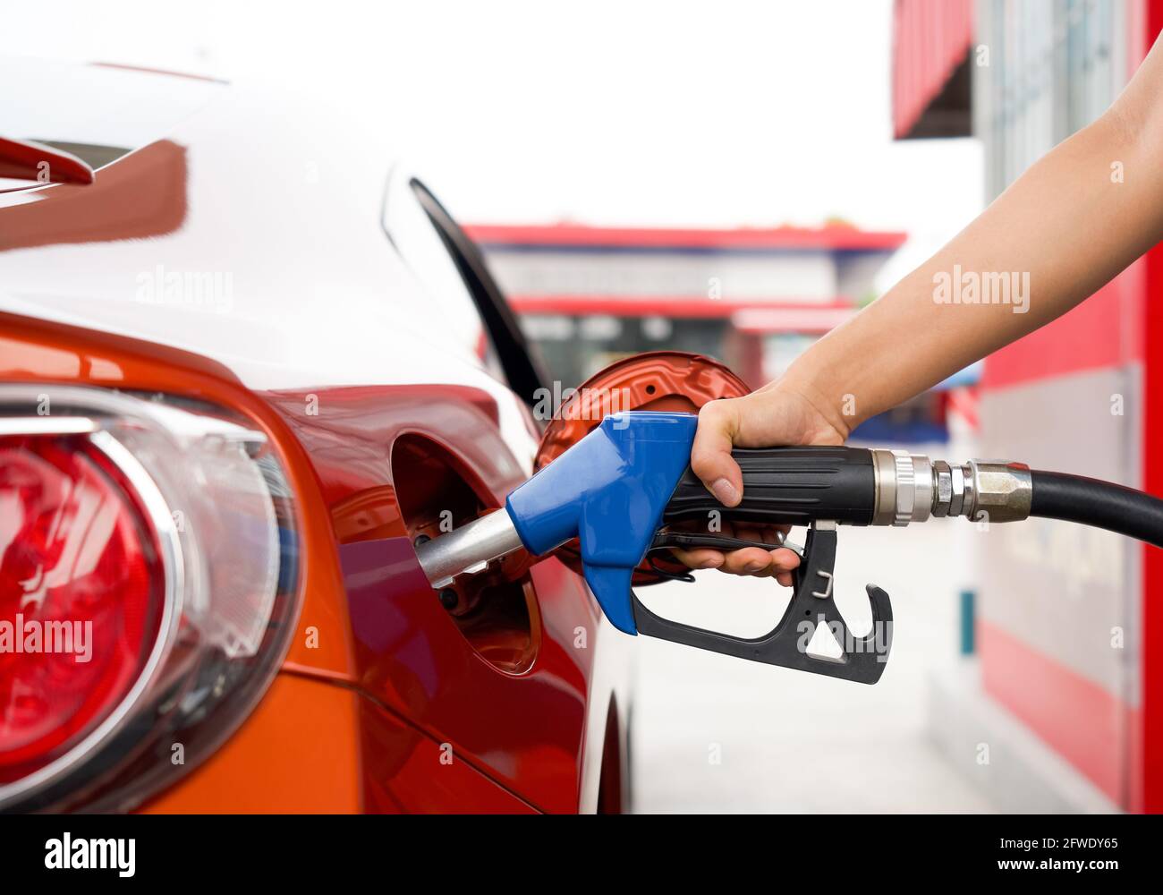 Gas station worker's hand holding blue benzene gas pump, filling up red ...