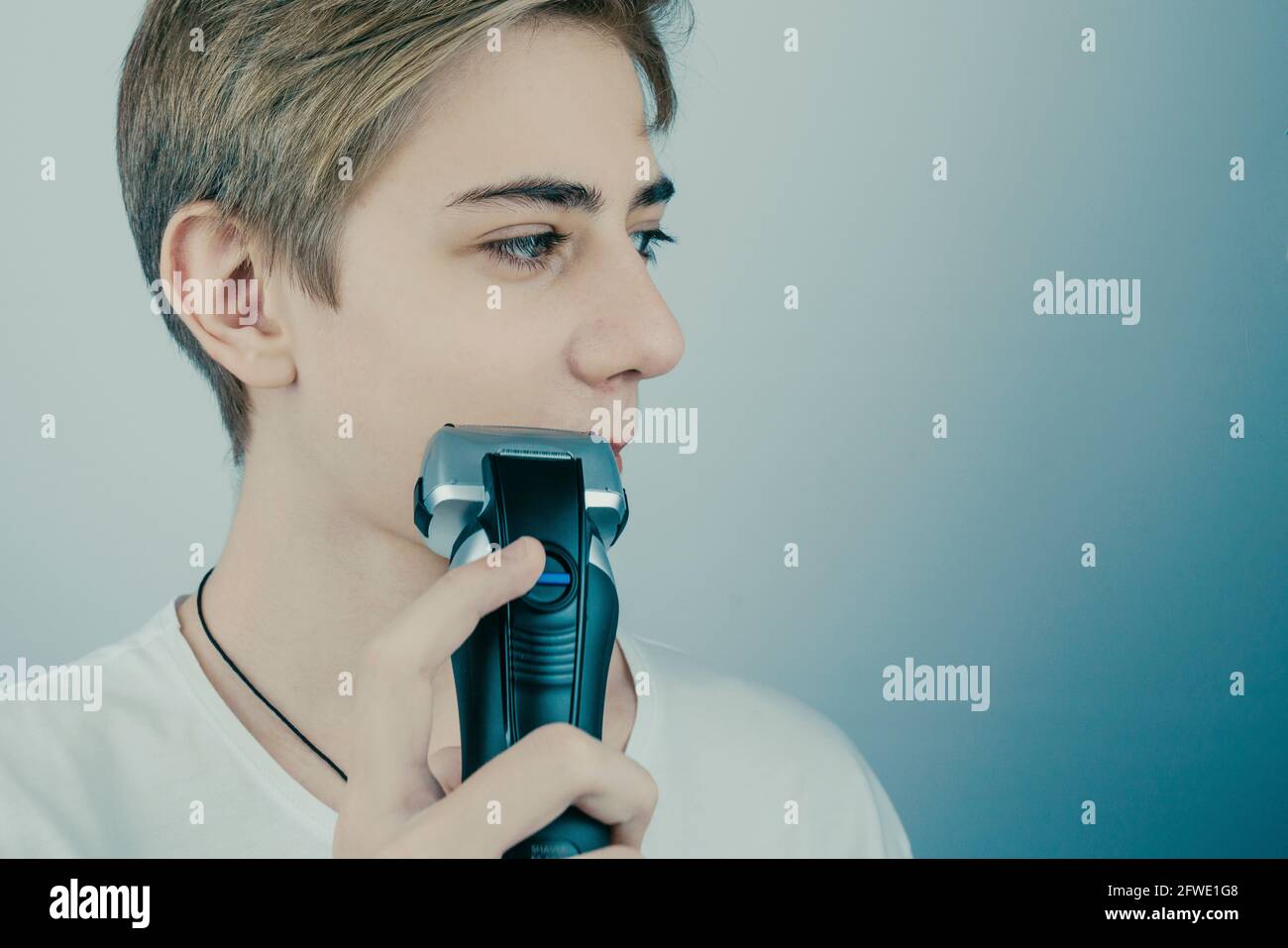 Portrait of a handsome smiling teenager in a white T-shirt shaves for ...