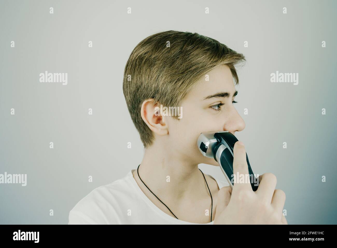Portrait of a handsome smiling teenager in a white T-shirt shaves for ...