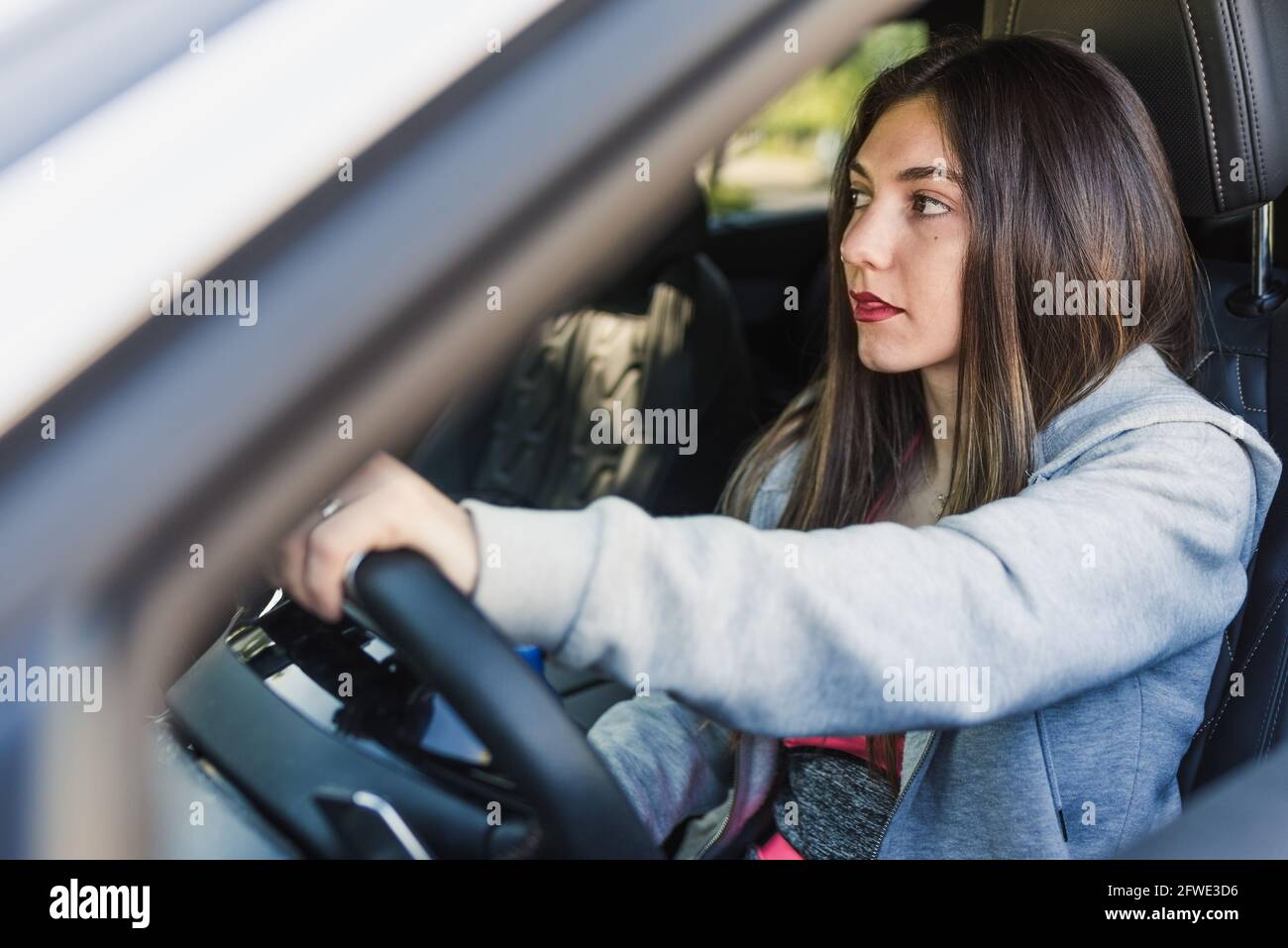 attractive caucasian woman driving a car seen from window. She wears ...
