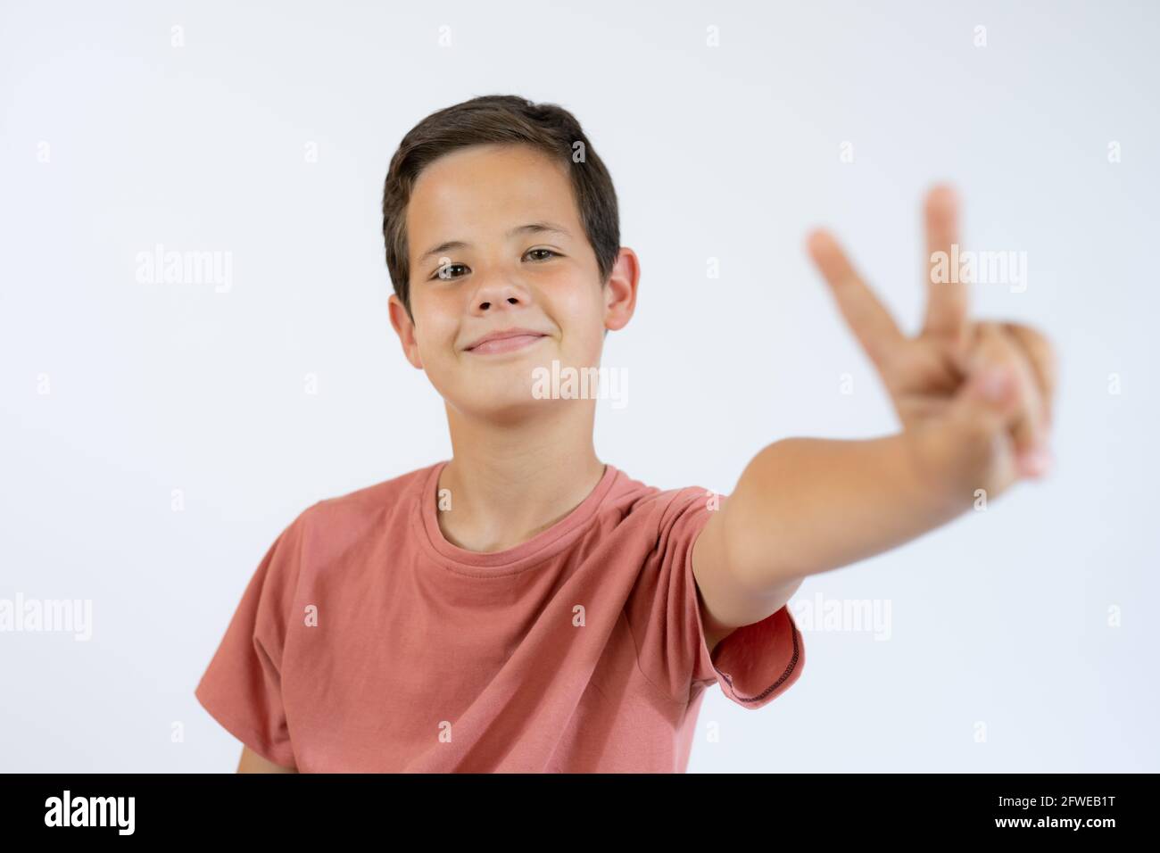 Portrait of little boy showing victory hand sign on white background ...