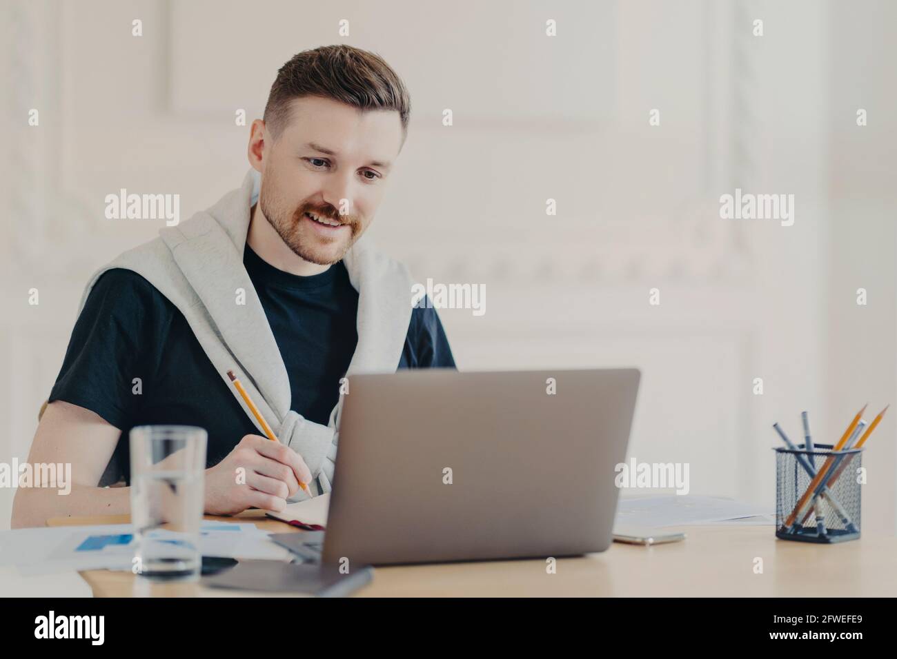Positive young freelancer taking notes during video call Stock Photo ...