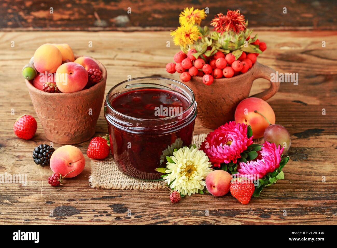 Jar of strawberry jam among summer and autumn fruits on a wooden table ...