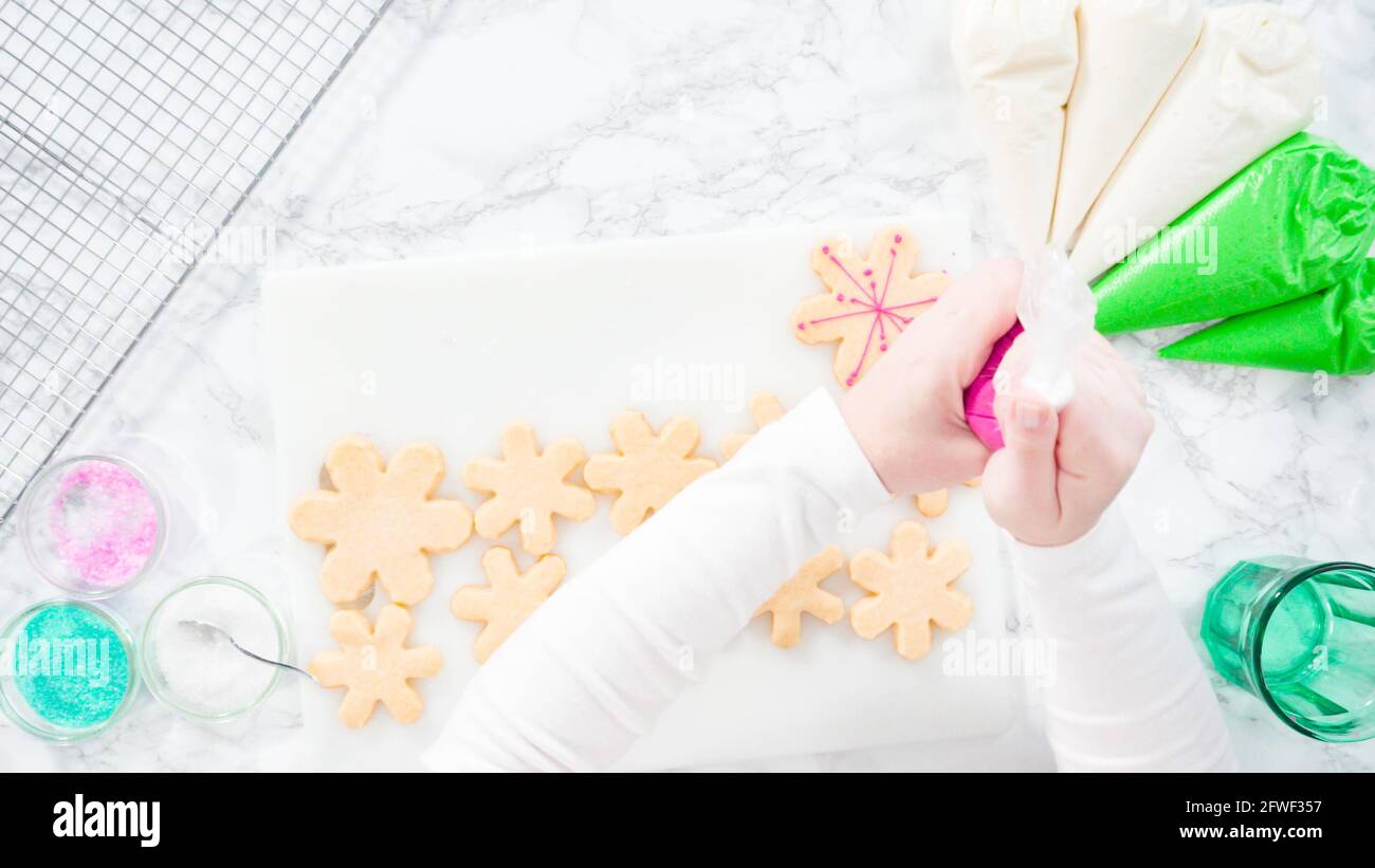 Flat lay. Stp by step. Icing snowflake shaped sugar cookies with pink ...
