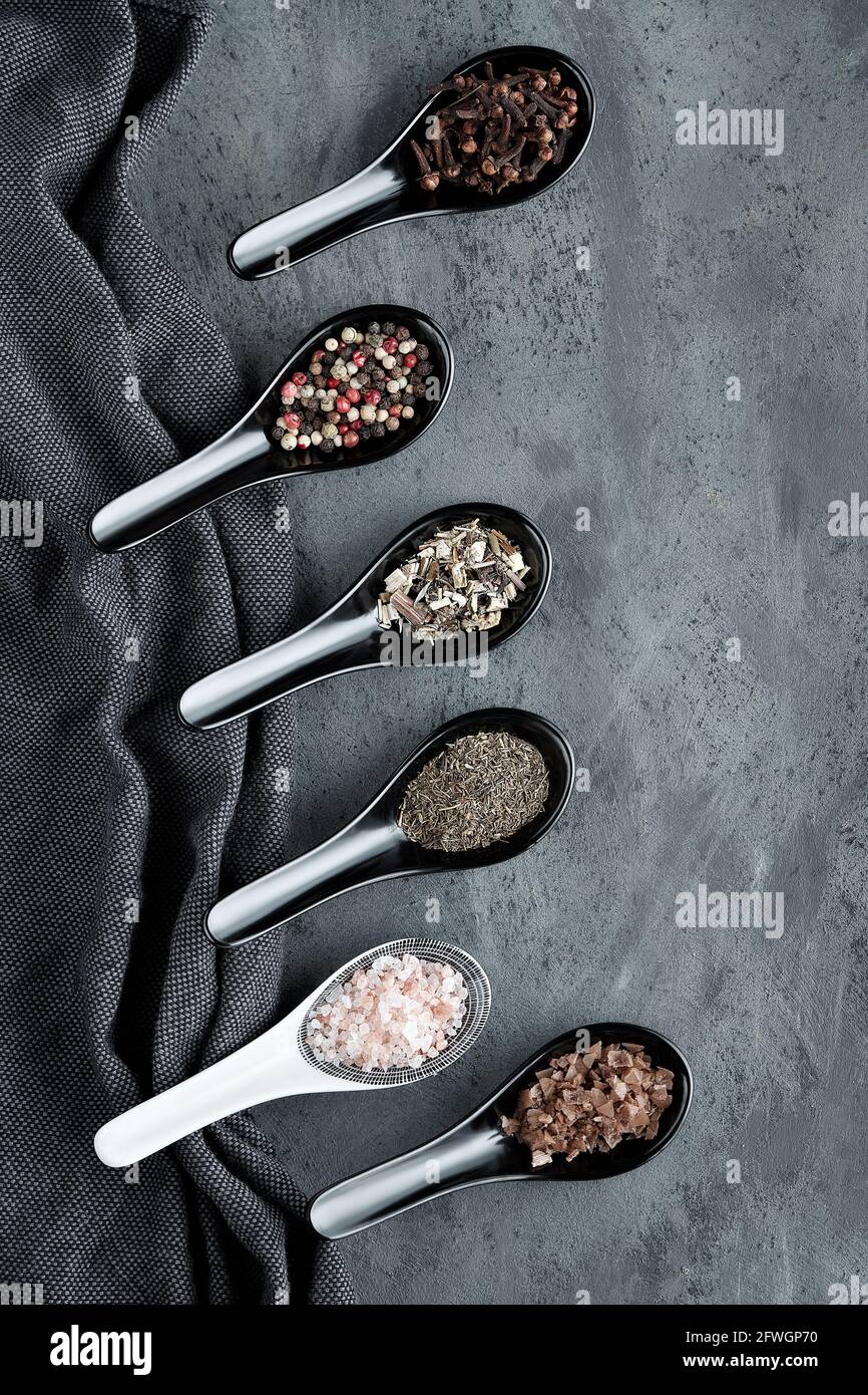 Various spices in ceramic oriental spoons and pinch bowls on dark grey ...