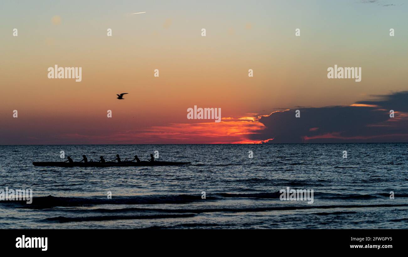 team rowing crew in silhouette on water against pastel sunset sky at ...