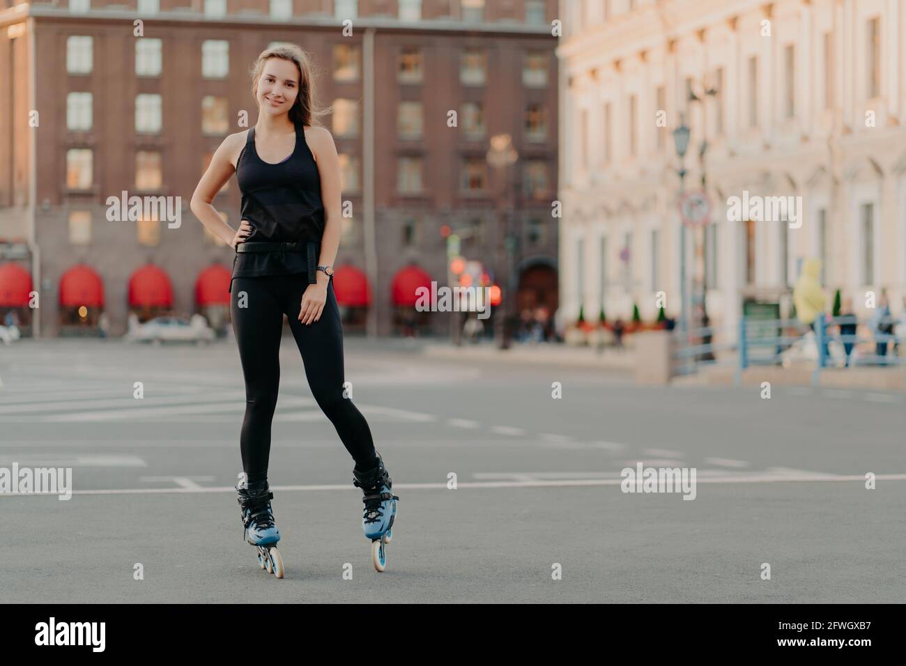 Horizontal shot of active woman practices rollerblading poses on blades ...