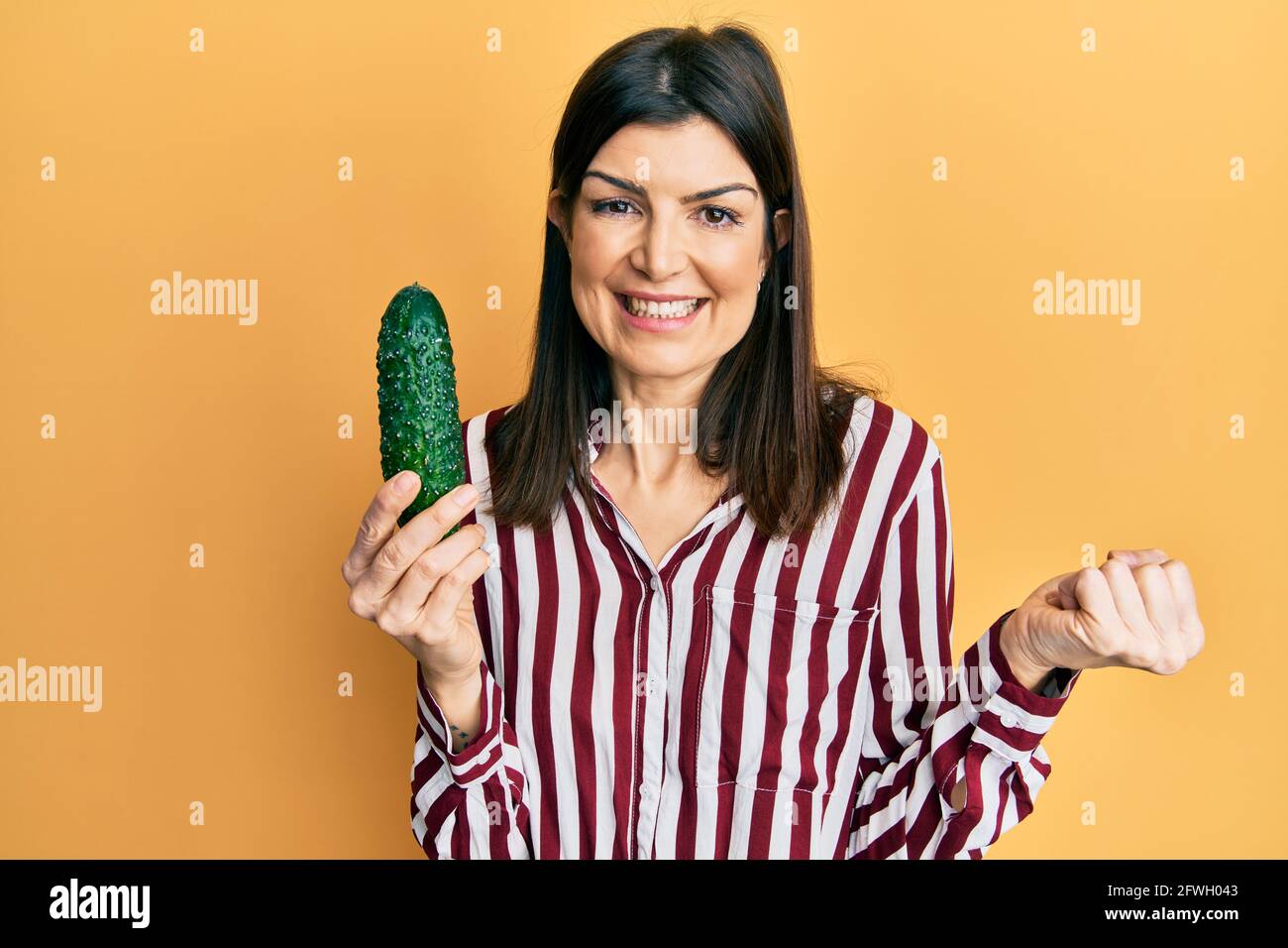 Young hispanic woman holding cucumber screaming proud, celebrating ...