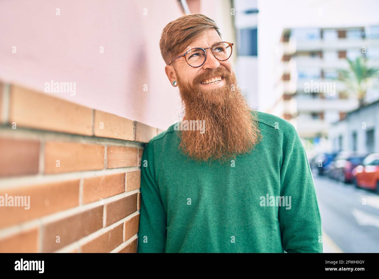 Young irish man with redhead beard smiling happy leaning on the wall at ...