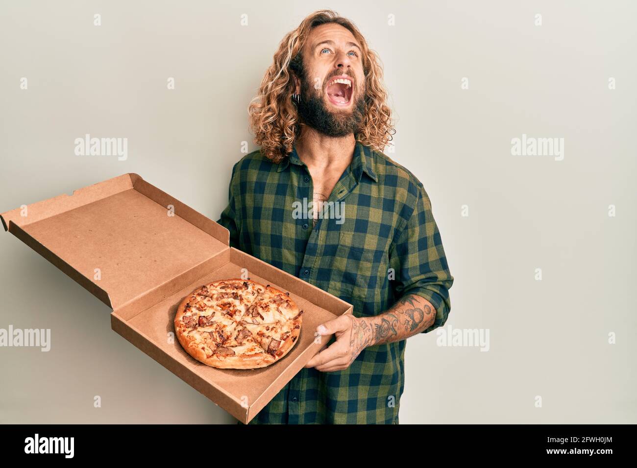 Handsome man with beard and long hair holding italian pizza angry and ...
