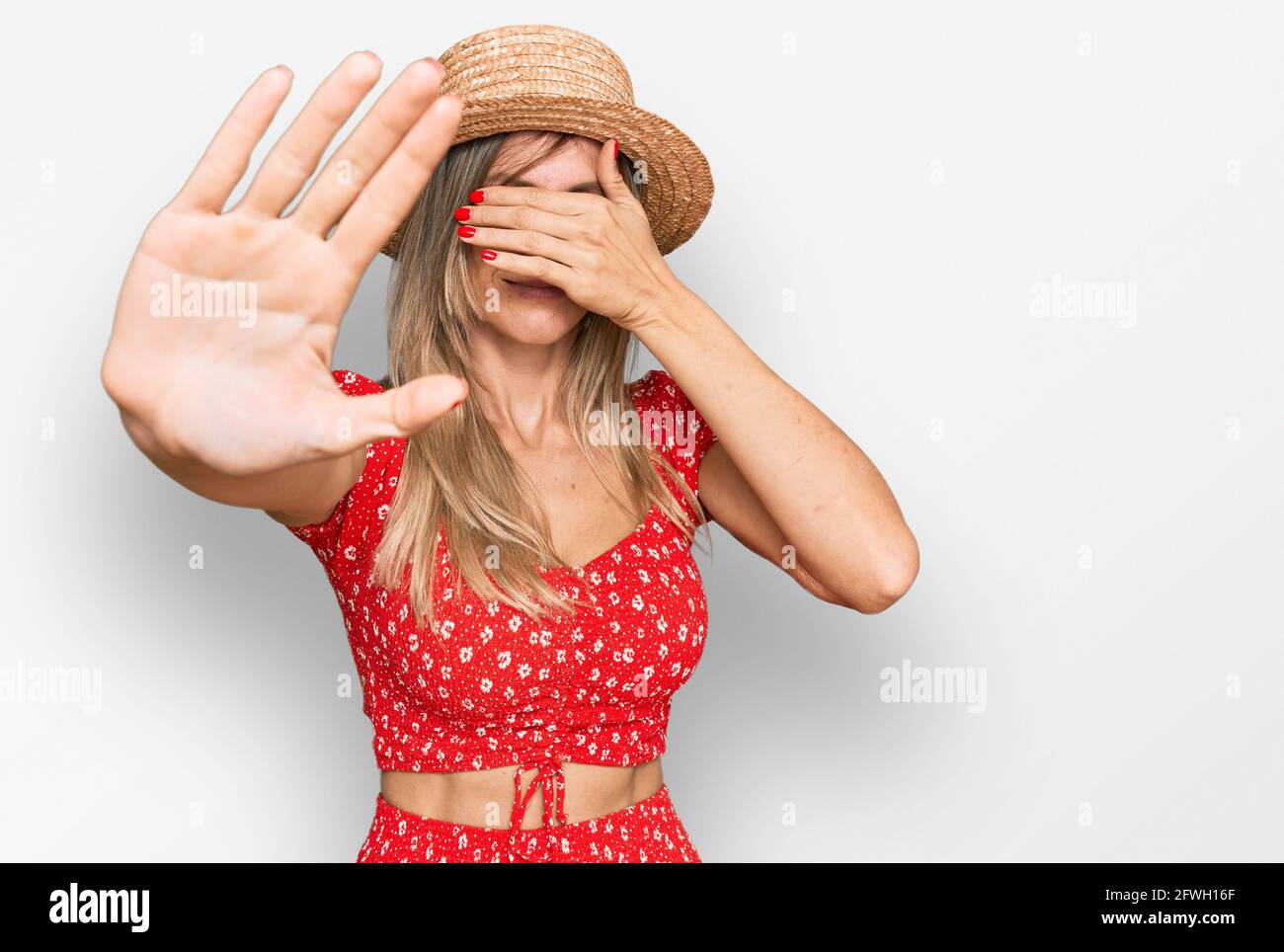 Beautiful caucasian woman wearing summer hat covering eyes with hands ...