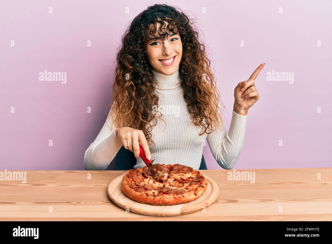 Young hispanic girl cutting tasty pepperoni pizza smiling happy ...