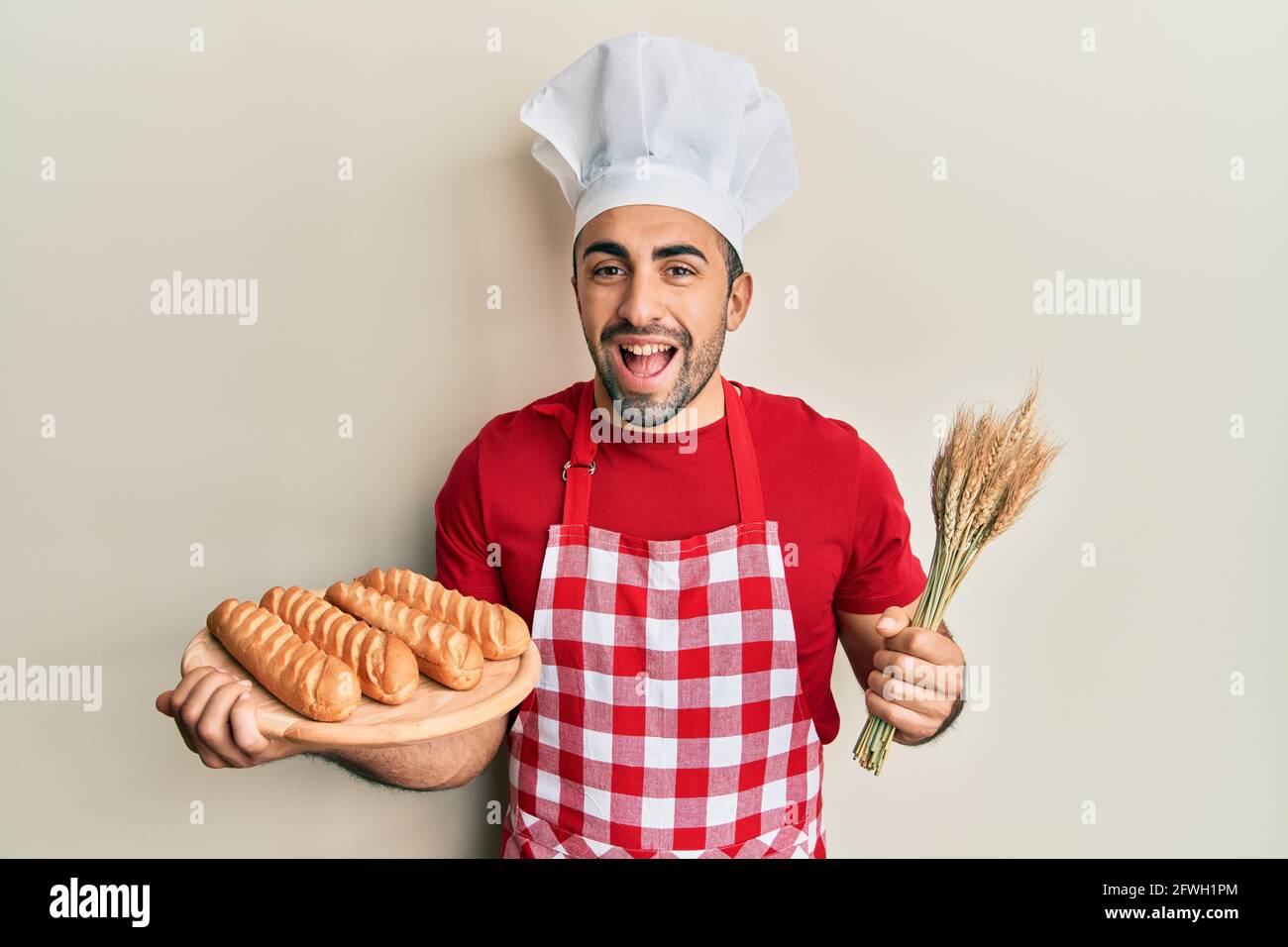Young hispanic man wearing baker uniform holding homemade bread and ...