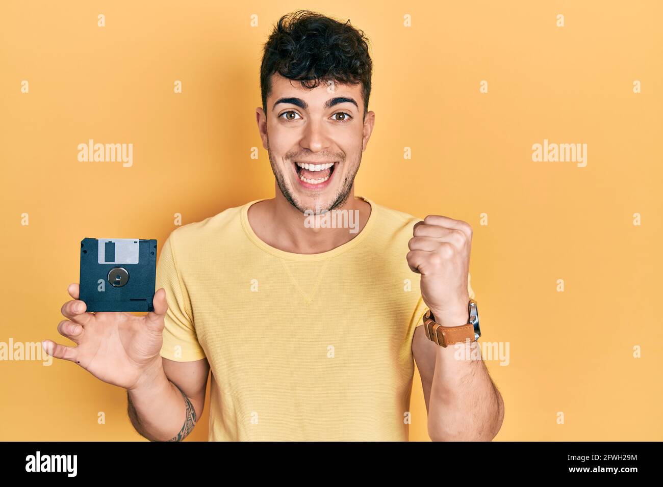 Young hispanic man holding floppy disk screaming proud, celebrating ...