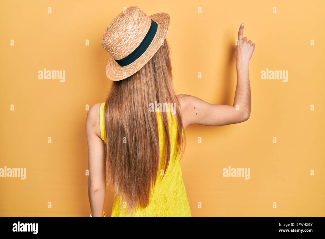 Young blonde girl wearing summer hat posing backwards pointing ahead ...