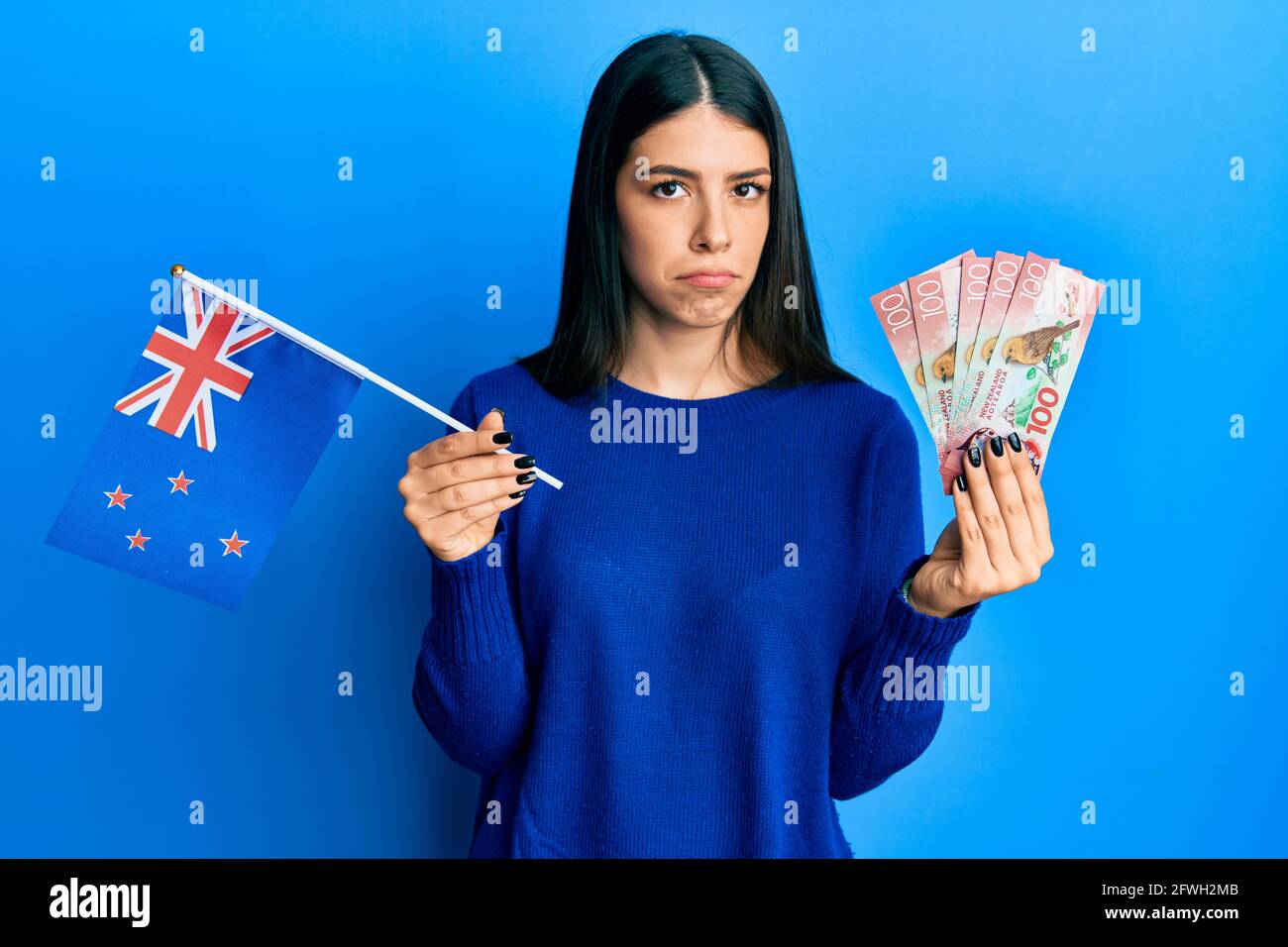 Young hispanic woman holding new zealand flag and dollars depressed and ...